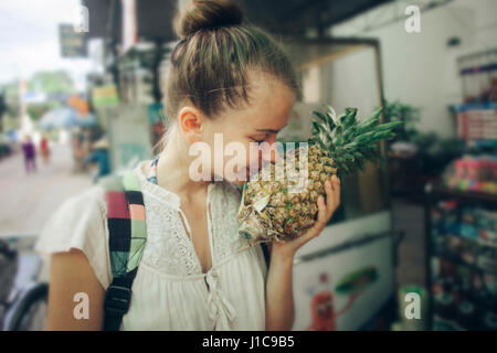 Smiling woman smelling fresh pineapple near asian friend in kitchen ...