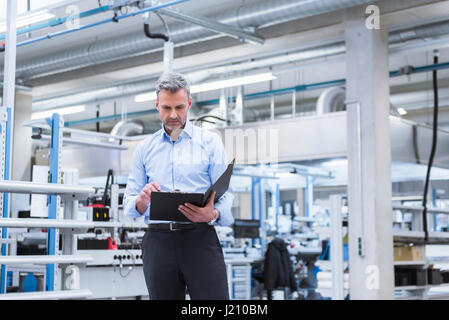 Businessman walking through shop floor, holding files Stock Photo - Alamy