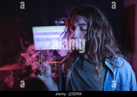 Male audio engineer smoking electronic cigarette in recording studio ...