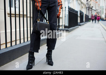 Low section of woman carrying shoulder bag while walking on footpath ...