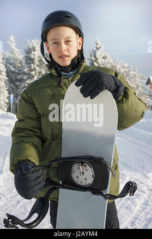 Portrait of a boy holding snowboard in snow aside and casual hat over ...