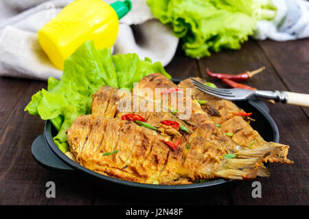 Fried fish carp (sazan) on a cast-iron frying pan with lettuce leaves ...