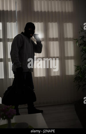 A robber with robbery mask holding a flashlight and piece of pipe ...