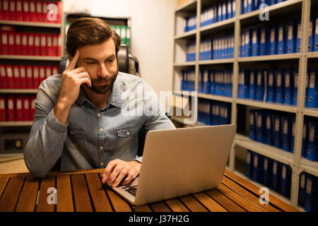 Thoughtful businessman with coffee cup and file folder leaning on wall ...