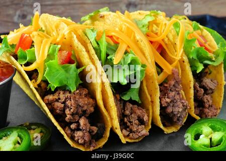 Hard shelled tacos with ground beef, lettuce, tomatoes and cheese close ...