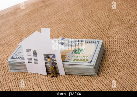 Paper house and a man figurine beside a bundle of US dollar banknote ...