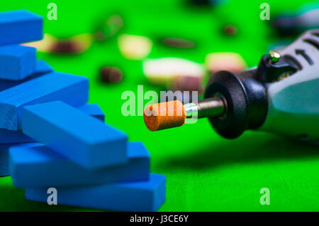 A gray drill with a small blue wooden pieces on a green background ...