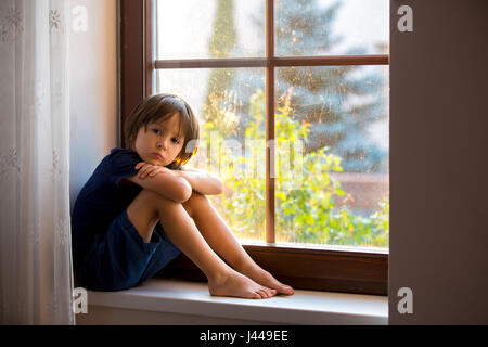 Sad boy sitting near window Stock Photo - Alamy