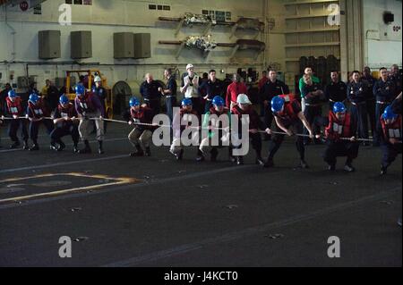 Senior enlisted Sailors haul in a messenger line in the hangar bay. The ...