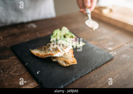 Chef decorate with vegetables dish of fried fish on wooden tray. Fresh ...