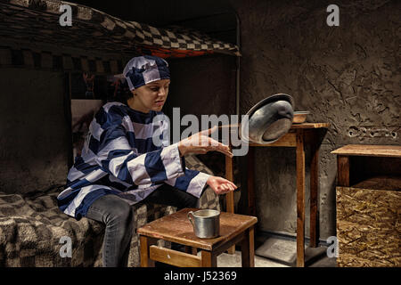 Angry female prisoner wearing prison uniform sitting on a bed and ...