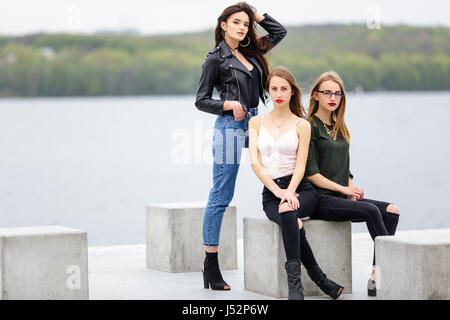 Two girls sit on bench with one stand near they, pose to camera Stock ...