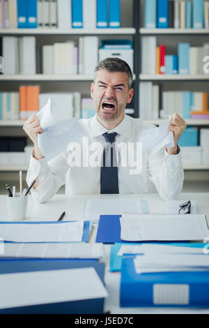 Angry nervous businessman working at office desk overloaded with ...