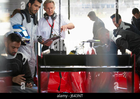Formula one driver watching pit crew repairing race car in repair ...