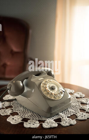 Vintage telephone on doily and wooden table in the living room next to ...