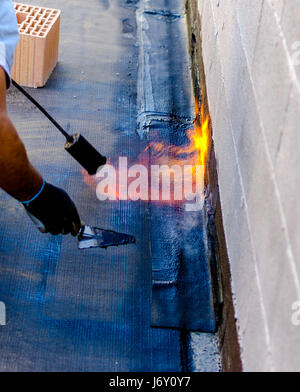 Roofer installing rolls of bituminous waterproofing membrane for the waterproofing of a terrace ...