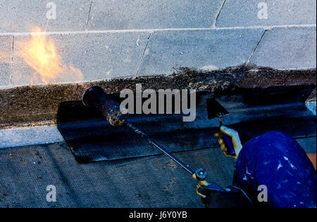 Roofer installing rolls of bituminous waterproofing membrane for the waterproofing of a terrace ...