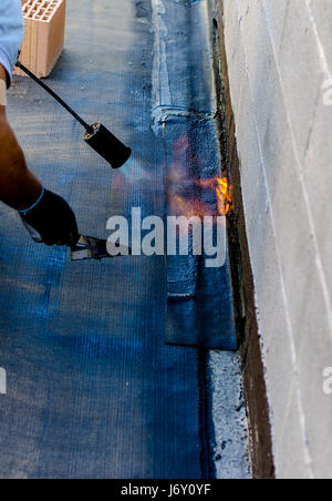 Roofer installing rolls of bituminous waterproofing membrane for the waterproofing of a terrace ...