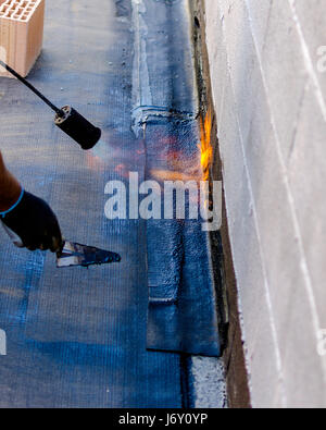 Roofer installing rolls of bituminous waterproofing membrane for the waterproofing of a terrace ...