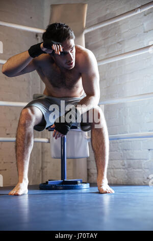 Tired boxer man wiping the sweat while sitting in the corner of boxing ...
