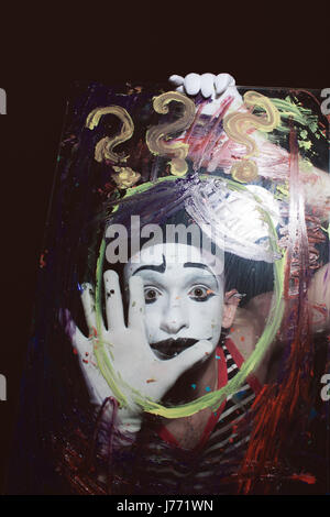 Face of Mime behind glass with multi-colored stains and question marks ...