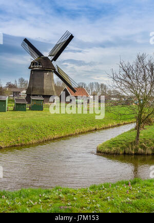 Historic windmill next to a church with green surroundings under a blue ...