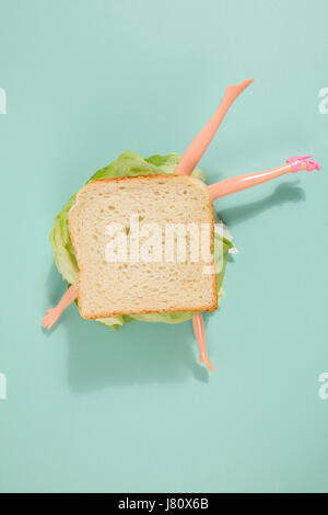 Parts of a doll's body in a sandwich with salad and soft bread on a ...