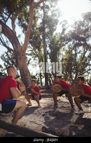 Trainer and kids carrying wooden logs during obstacle course training ...