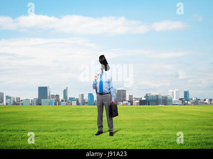 Camera headed man standing on green grass against modern cityscape ...