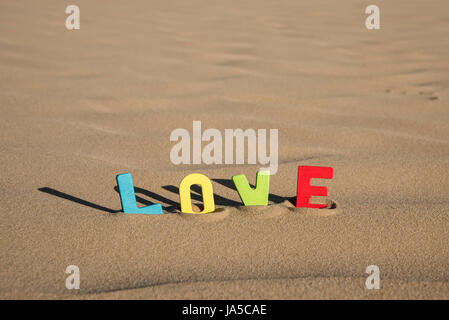 LOVE written out with colourful wooden letters text on sand of a dune ...