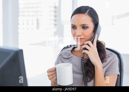 Serious secretary answering phone in her office and looking at camera ...