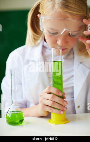 Chemistry student smelling test tube with colorful liquid sitting in ...