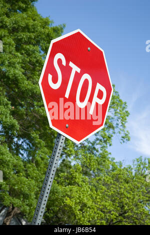 A red octagon-shaped stop sign in front of a white building with lush ...