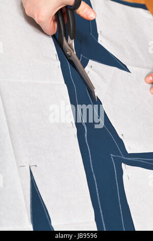 The tailor cuts out the fabric according to the pattern, close up ...