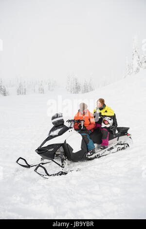 Couple having coffee from thermos while relaxing on snowmobile during ...
