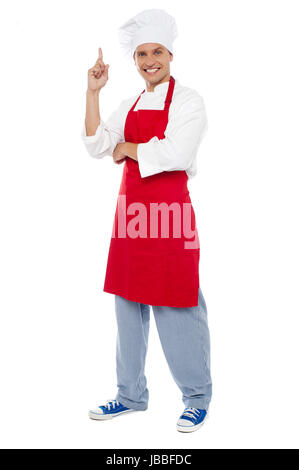 Young smart chef pointing index finger upwards. Full length portrait ...