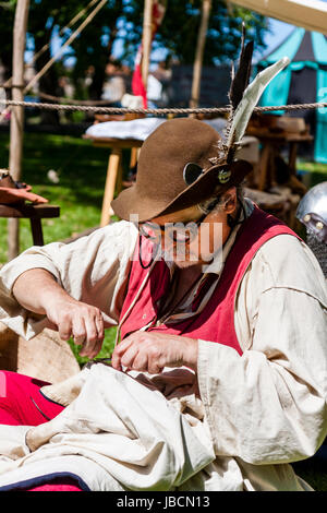 Re-enactment, Medieval weaver, with glasses, sitting on grass while ...