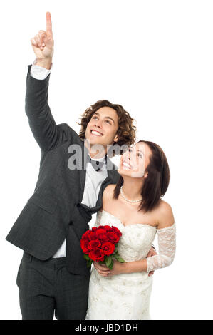 Cheerful groom pointing with finger at bride while walking in park ...
