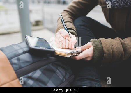 Cropped hand writing in notebook with laptop and smartphone for remote ...