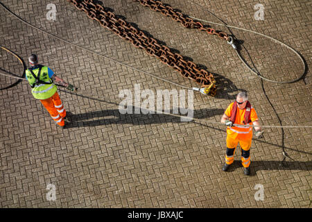 Dockworkers attaching moored ship's hawser to shoreside bitt in seaport ...