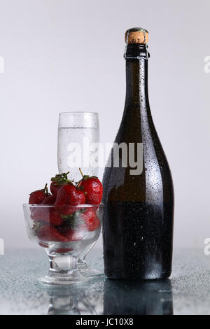Champagne bottle with chilled class and strawberies on a wet light ...