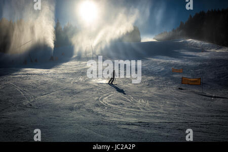 Professional skier going down the slope under working snow cannons ...