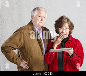 Suspicious man and embarrassed woman holding tablet Stock Photo - Alamy