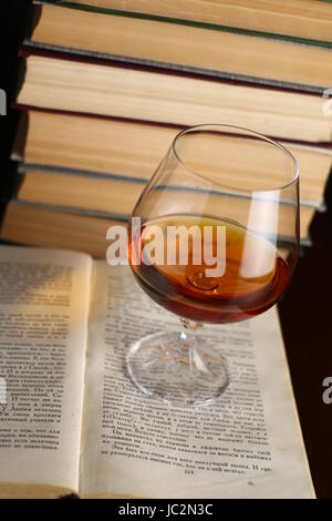 Glass of brandy standing on open books Stock Photo - Alamy