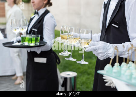 Midsection of professional waiters in uniform serving wine, cocktails ...