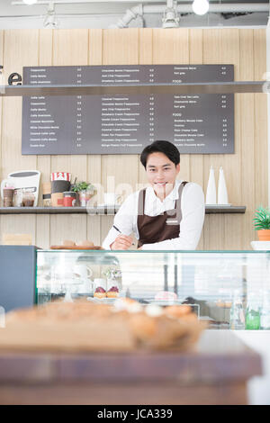 Young man smiling in a bakery, wearing an apron with arms crossed ...