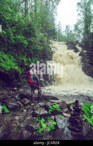 Traveler with a backpack near waterfall. It's raining Stock Photo - Alamy