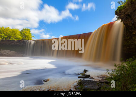 A long exposure shot of a waterfall flowing over rocks in a forest ...