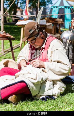 Re-enactment, Medieval weaver, with glasses, sitting on grass while ...