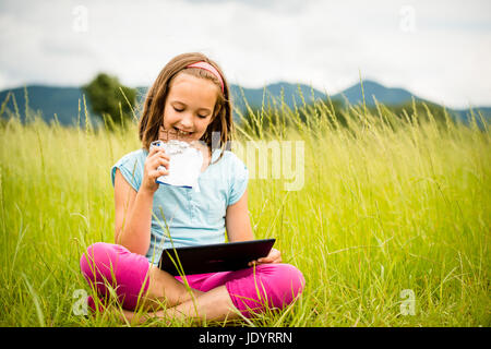 Child eating and relishing chocolate while watching tablet - outdoor in ...